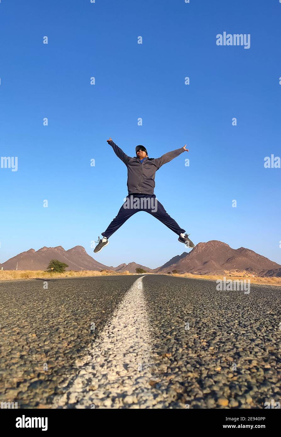 Vertical shot of an Asian happy man jumping in the middle of a road ...