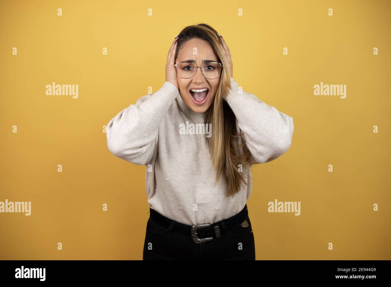 Pretty woman with long hair crazy and scared with hands on head, afraid ...