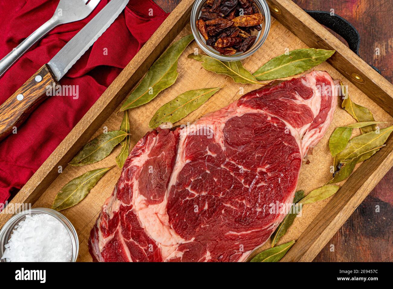 Raw beef ribeye on a round slate plate with glass containers containing ...