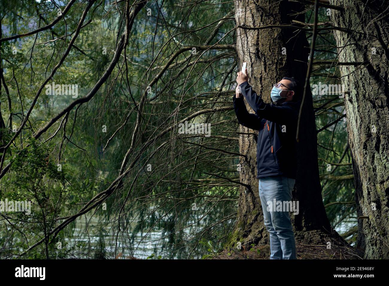 Young man taking a photo of the view in a forest while wearing a face ...