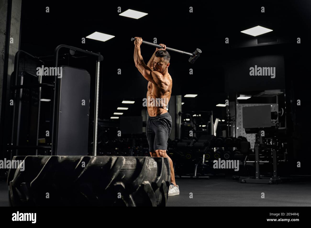 Side view of powerful muscular man hitting giant tire with sledgehammer ...