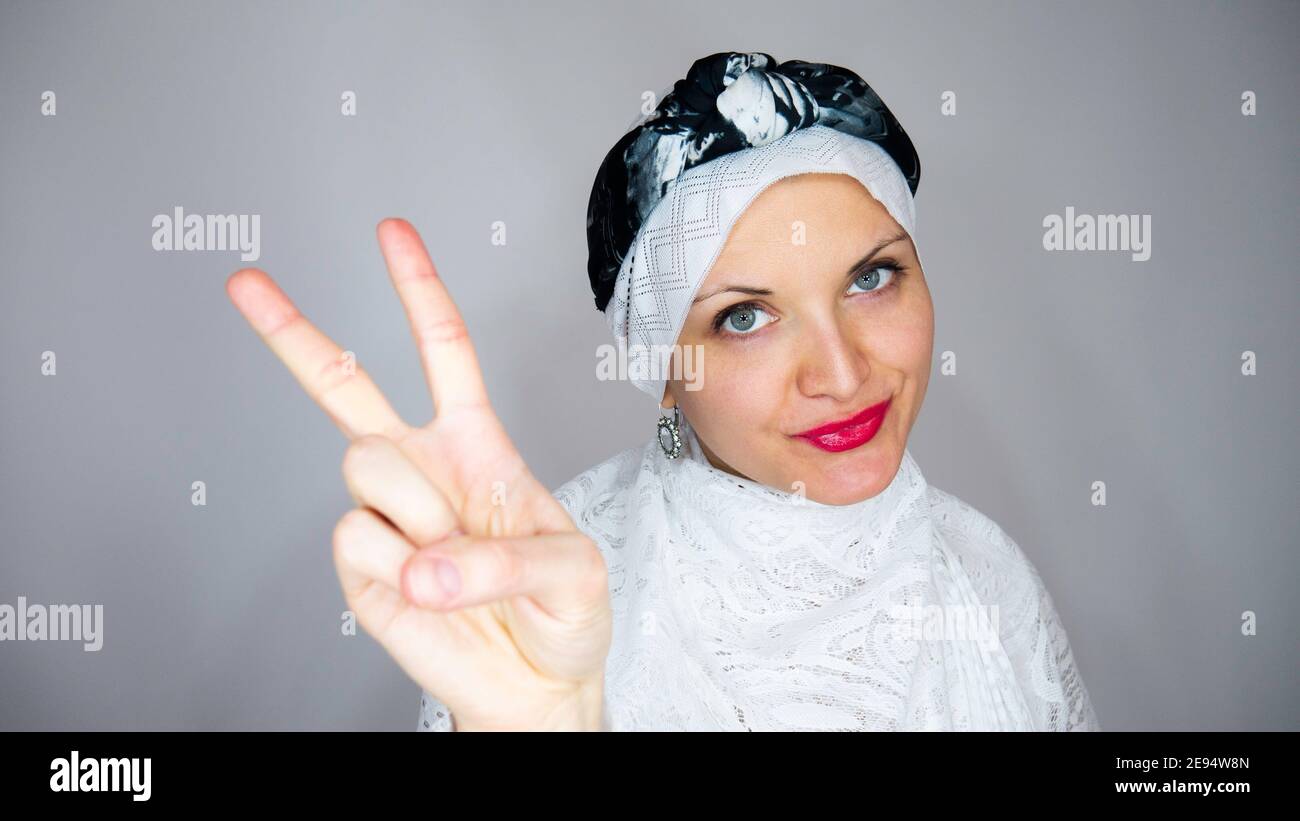 A Muslim woman in white gives a sign of peace on a white background ...