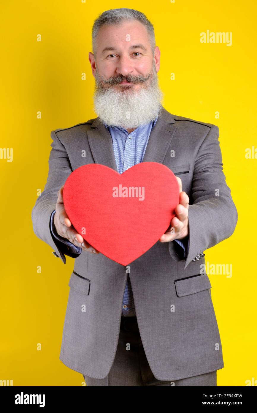 Studio portrait of mature bearded man holding out heart shape gift box ...