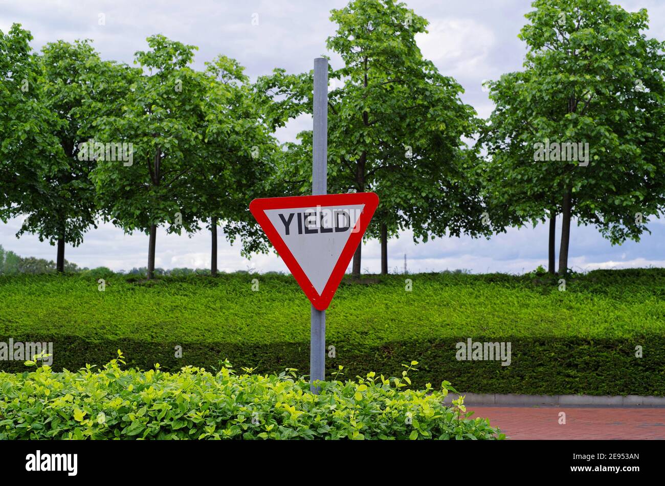 Closeup of a red triangle "YIELD" sign in a park under a cloudy sky ...