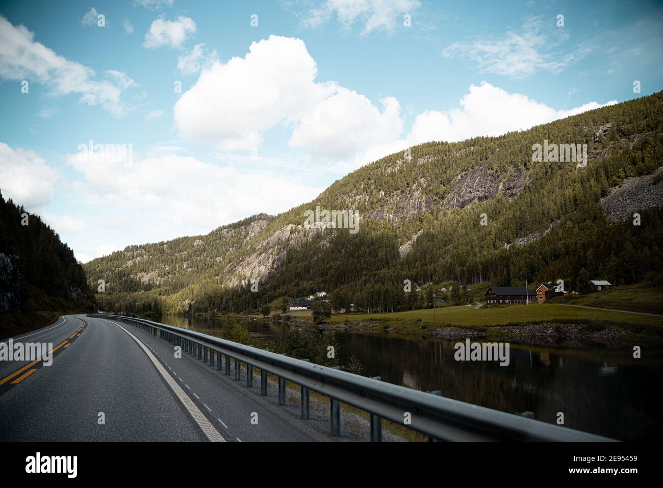 Closeup shot of an asphalt road on the edge of a river and a village on ...
