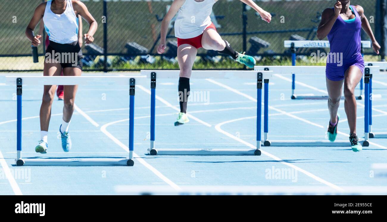 Three high school girls competing in a four hundred meter hurdle race ...