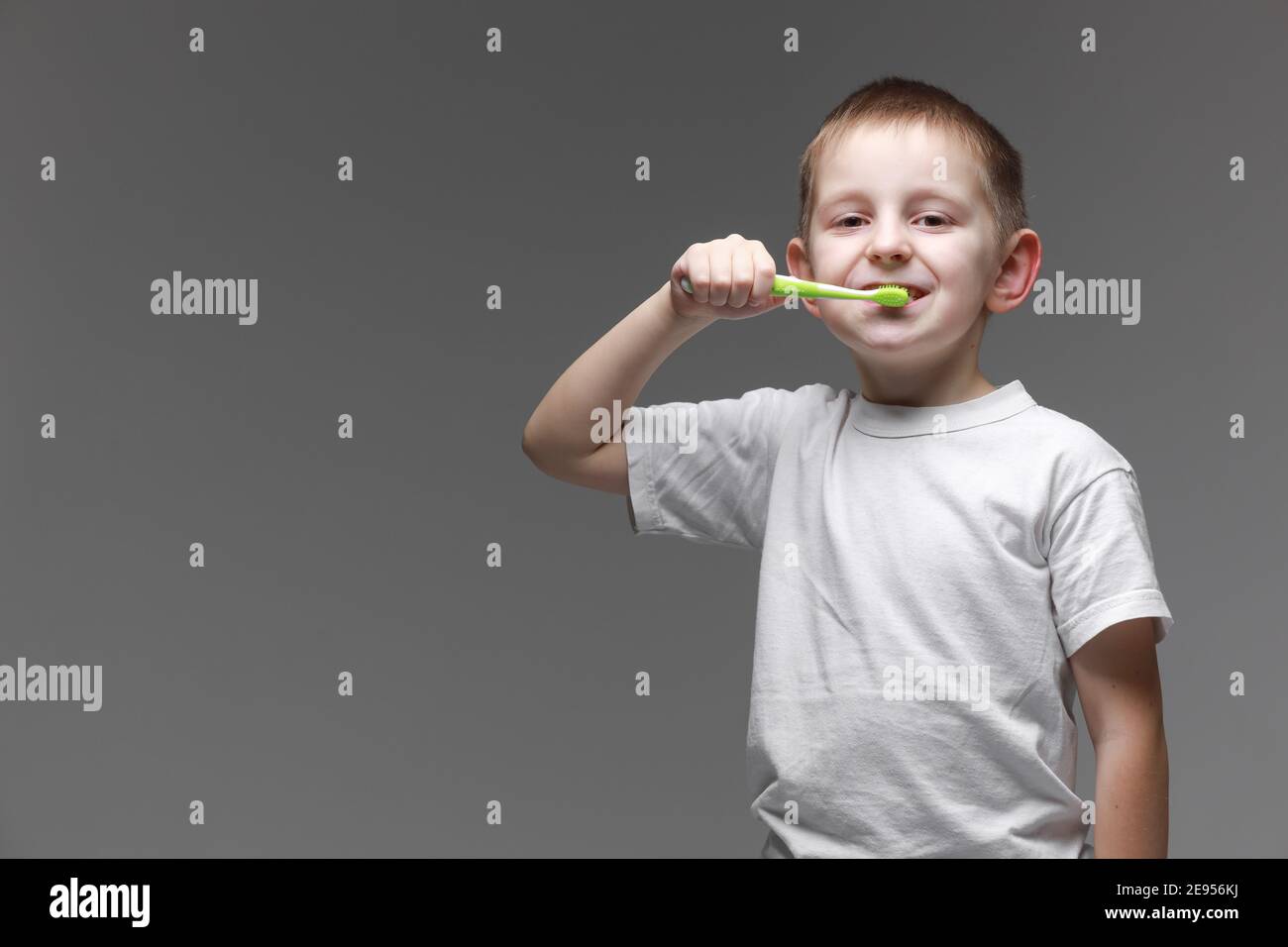 Happy child kid boy brushing teeth with toothbrush on gray background ...