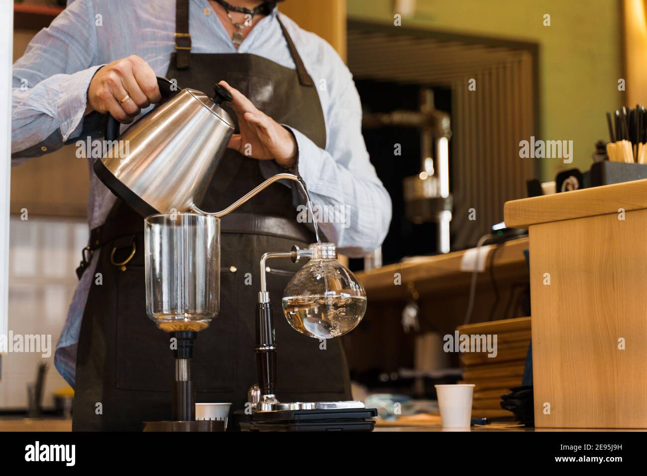 Close-up barista pours hot boiling water from kattle in glass syphon ...