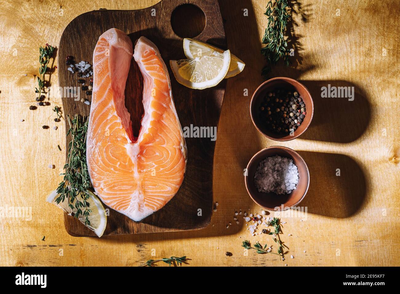 Raw salmon steak with lemon and thyme on wooden board, top view. Harsh ...