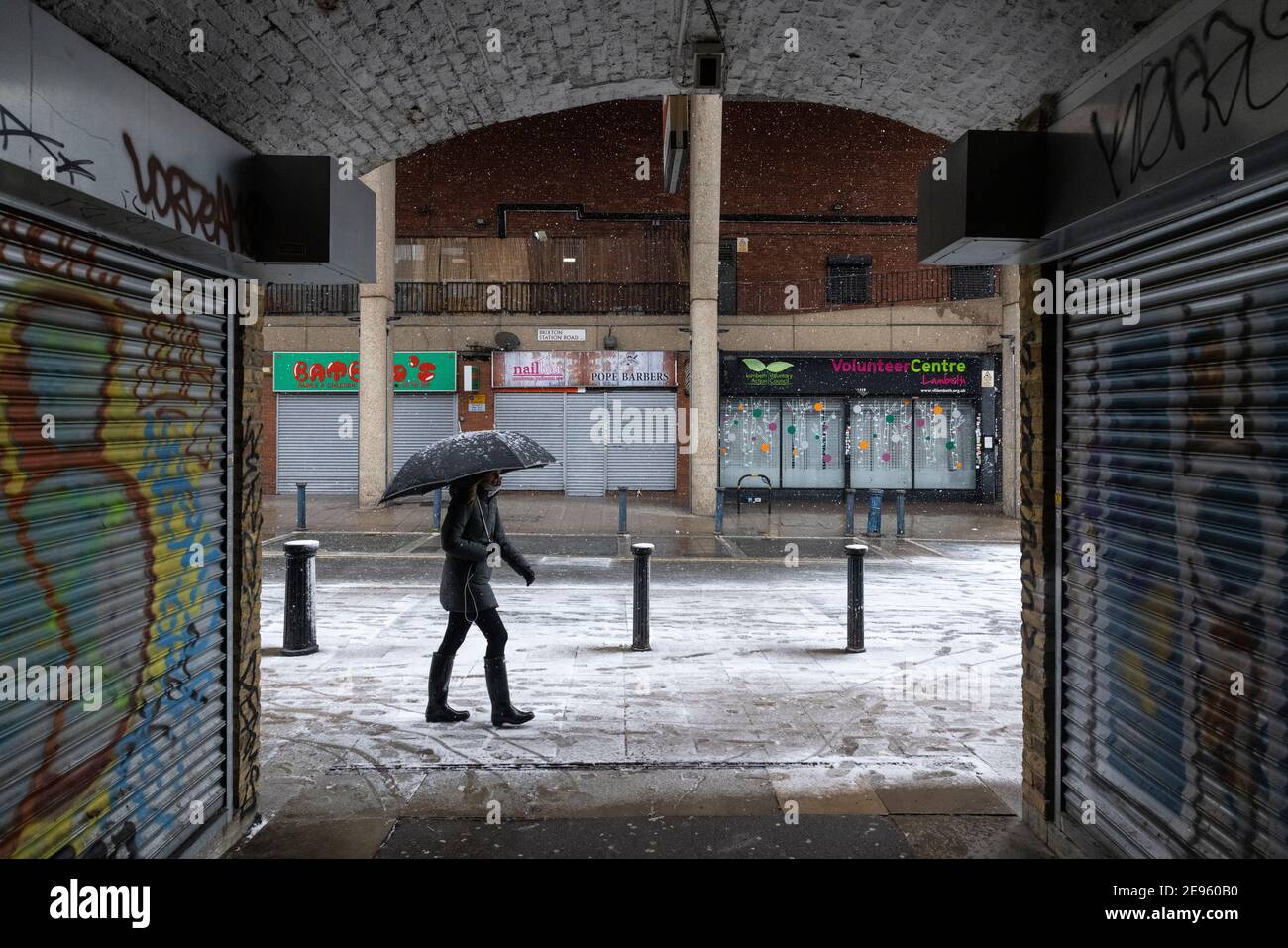 A woman with umbrella walks past entrance to Brixton Station during ...