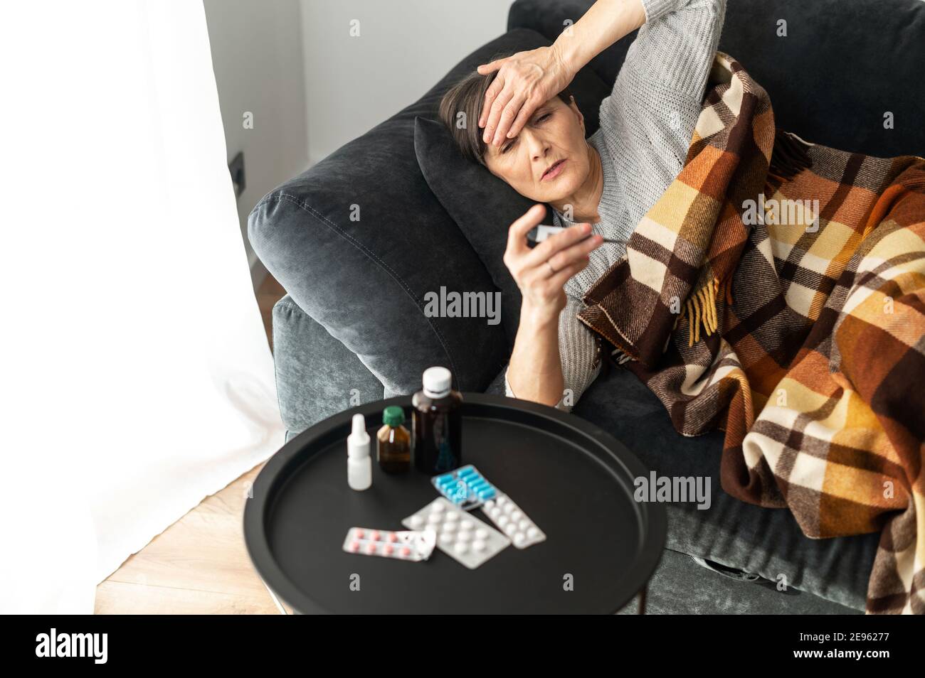 Sick senior woman has fever, cold and flu symptoms, lays on the couch ...