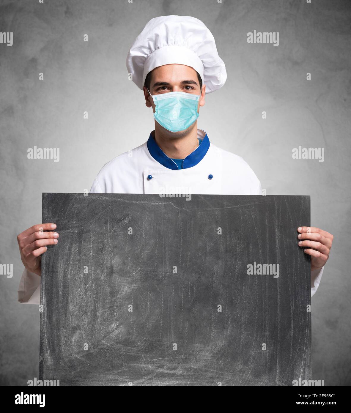 Masked chef or cook holding a blackboard during covid coronavirus ...