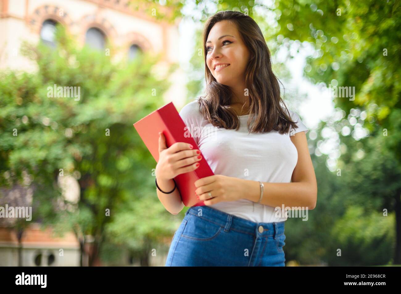 Beautiful female student holding a book outdoor Stock Photo - Alamy