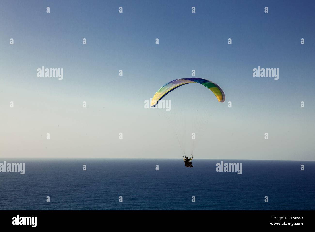 Blue and red paragliding parachute on light blue sky with copy space ...