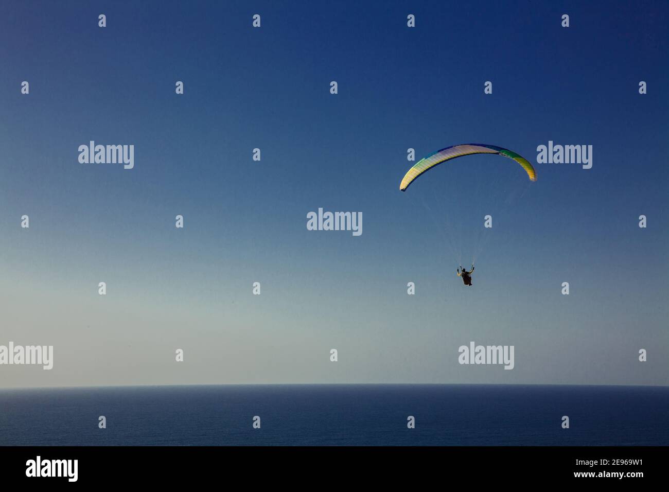 Blue and red paragliding parachute on light blue sky with copy space ...