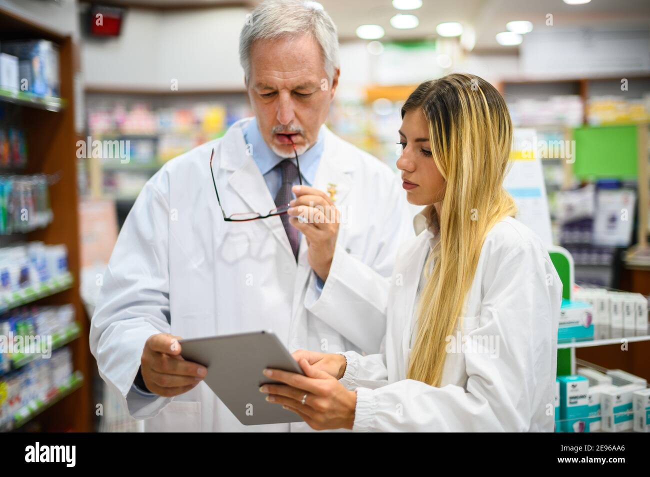 Two pharmacists talking while working on tablet in their store Stock ...