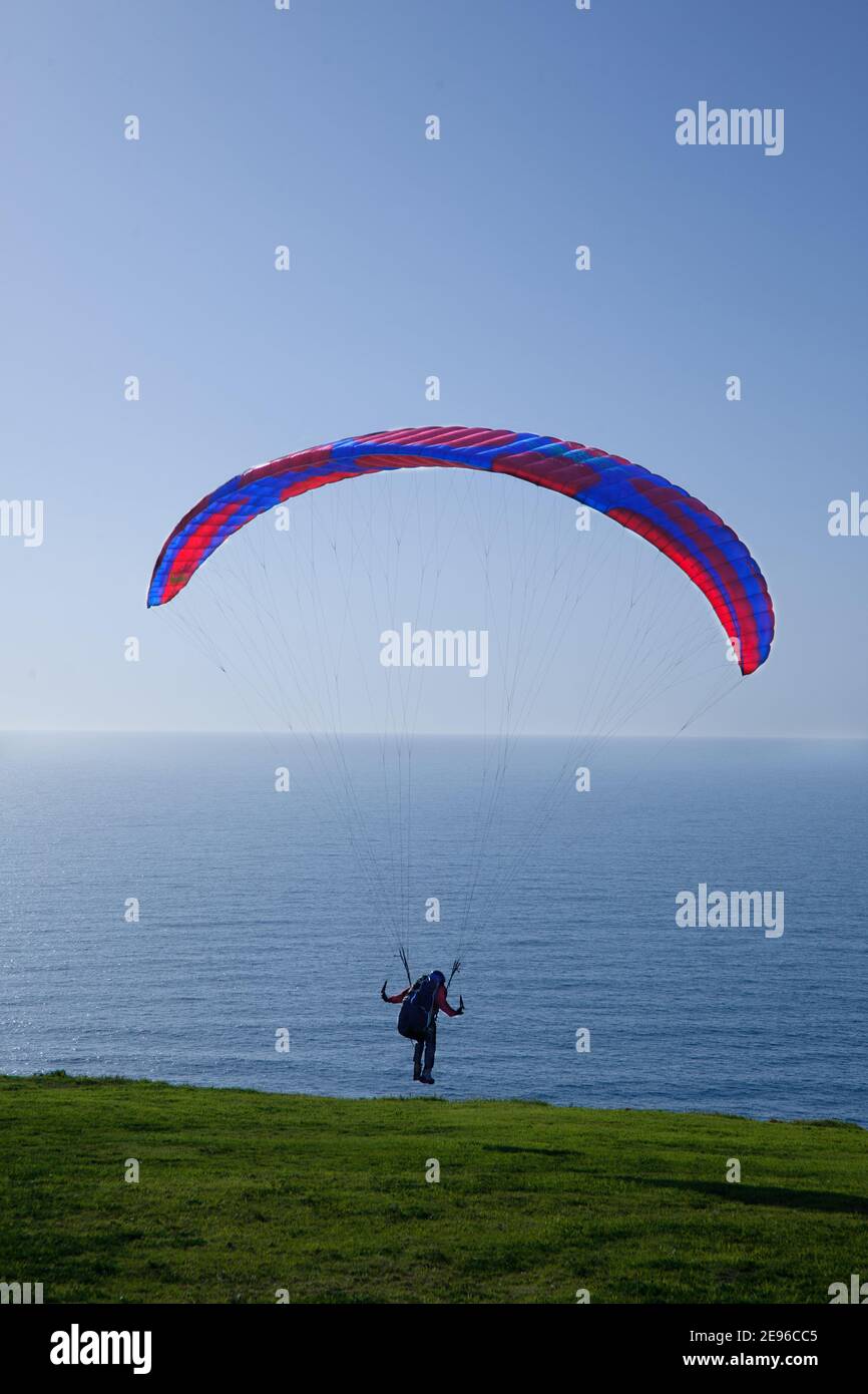 Blue and red paragliding parachute on light blue sky with copy space ...
