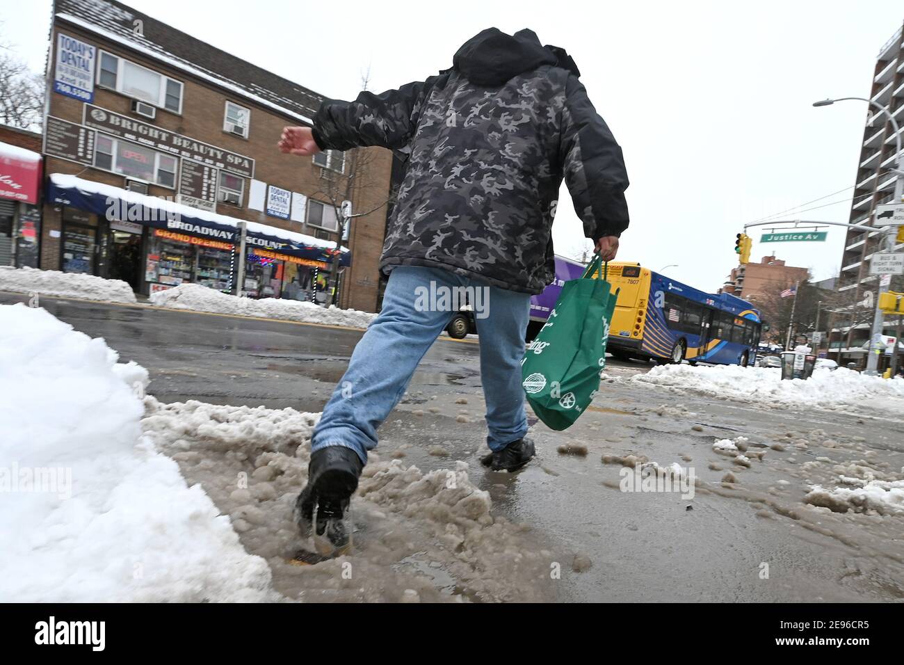 A man steps into a deep puddle of melted snow at a crosswalk after a ...