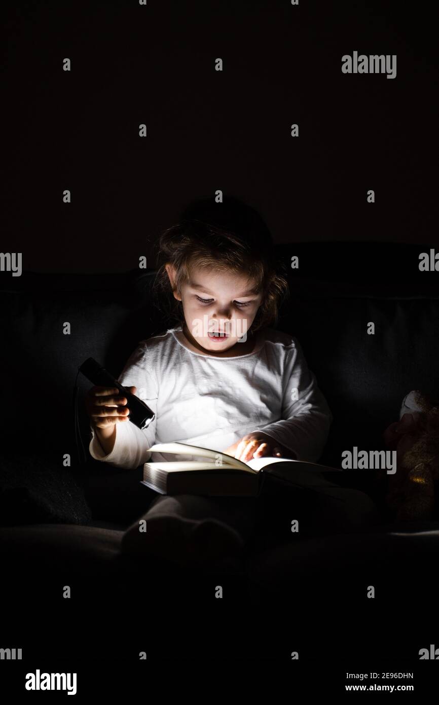 toddler caucasian girl reading book at hight with flashlight. Unplugged ...