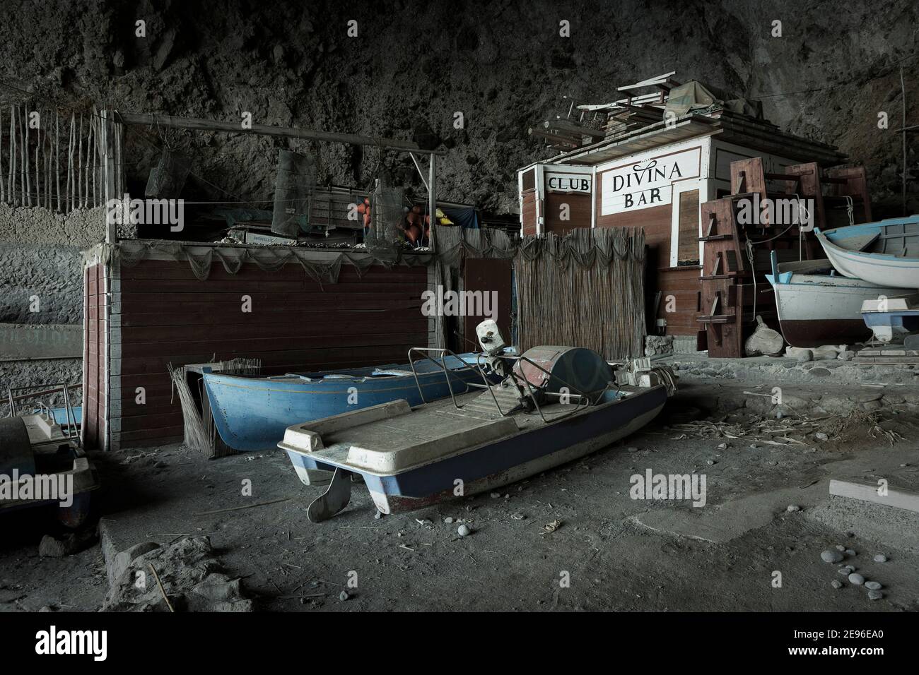 Dusty beach cave carved out of cliff in off season with beached boats ...