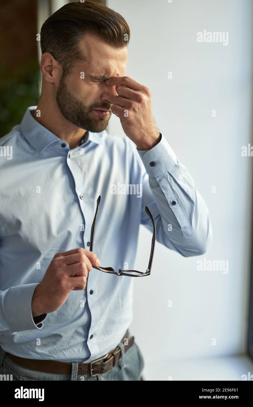 Young handsome man taking the glasses off and touching his aching eyes ...