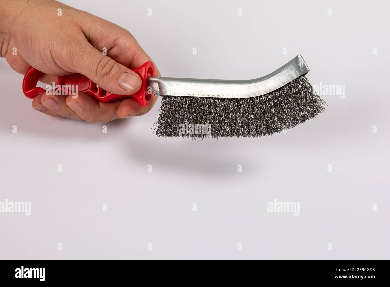 Metal wire brush with red plastic handle in a man's hand. White ...