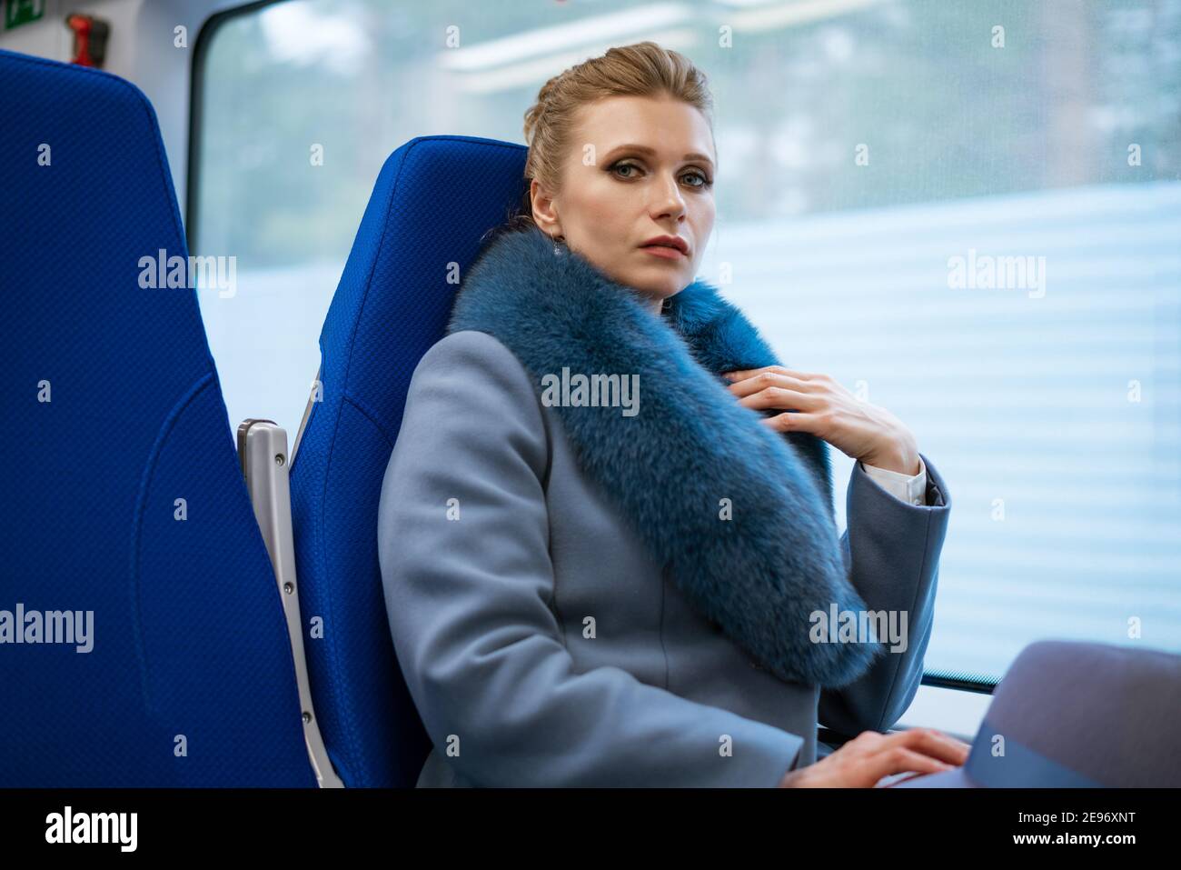 beautiful blonde woman with makeup in a blue coat rides in the train ...