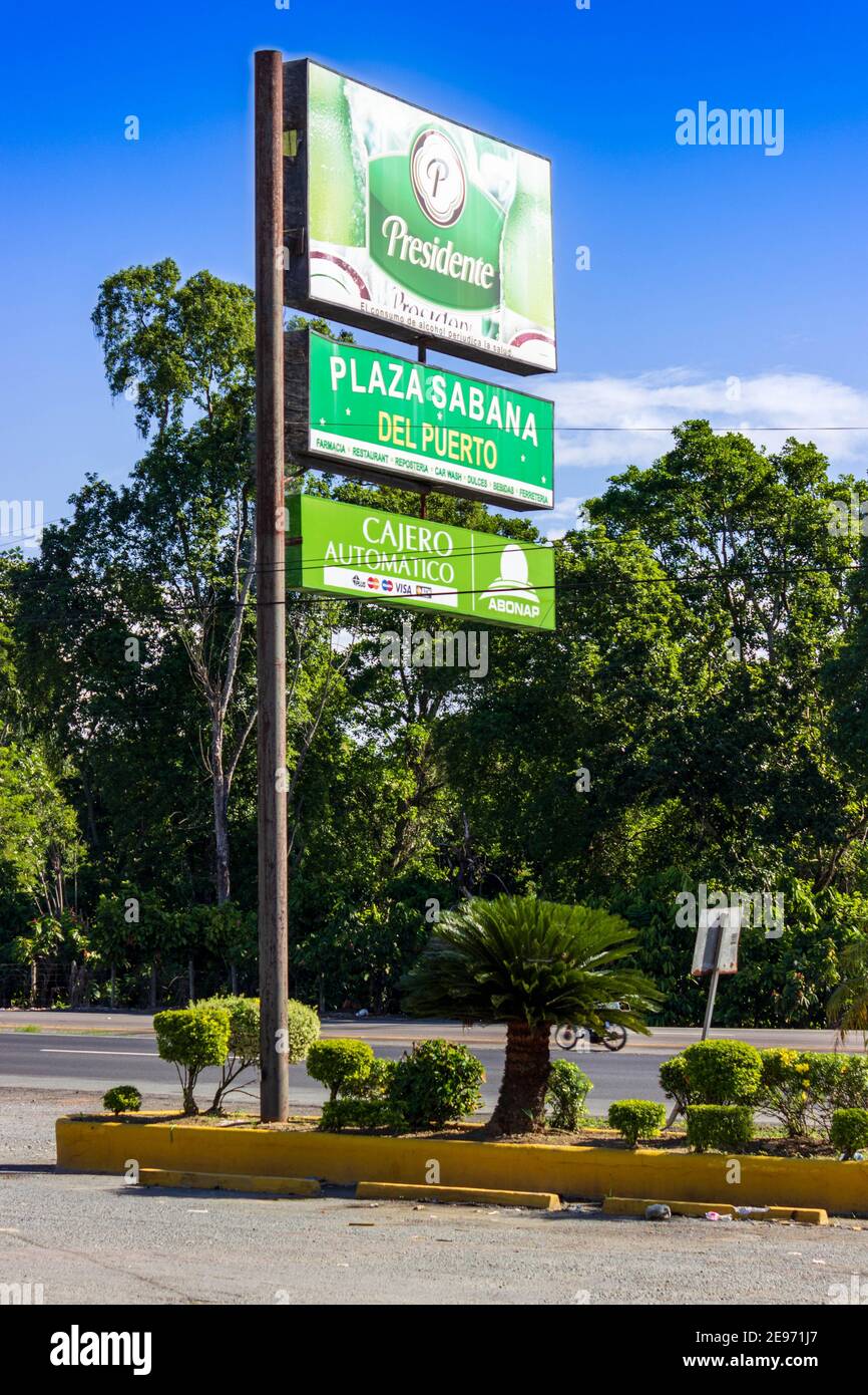 A convenience store sign stands alongside the road amid palms and ...