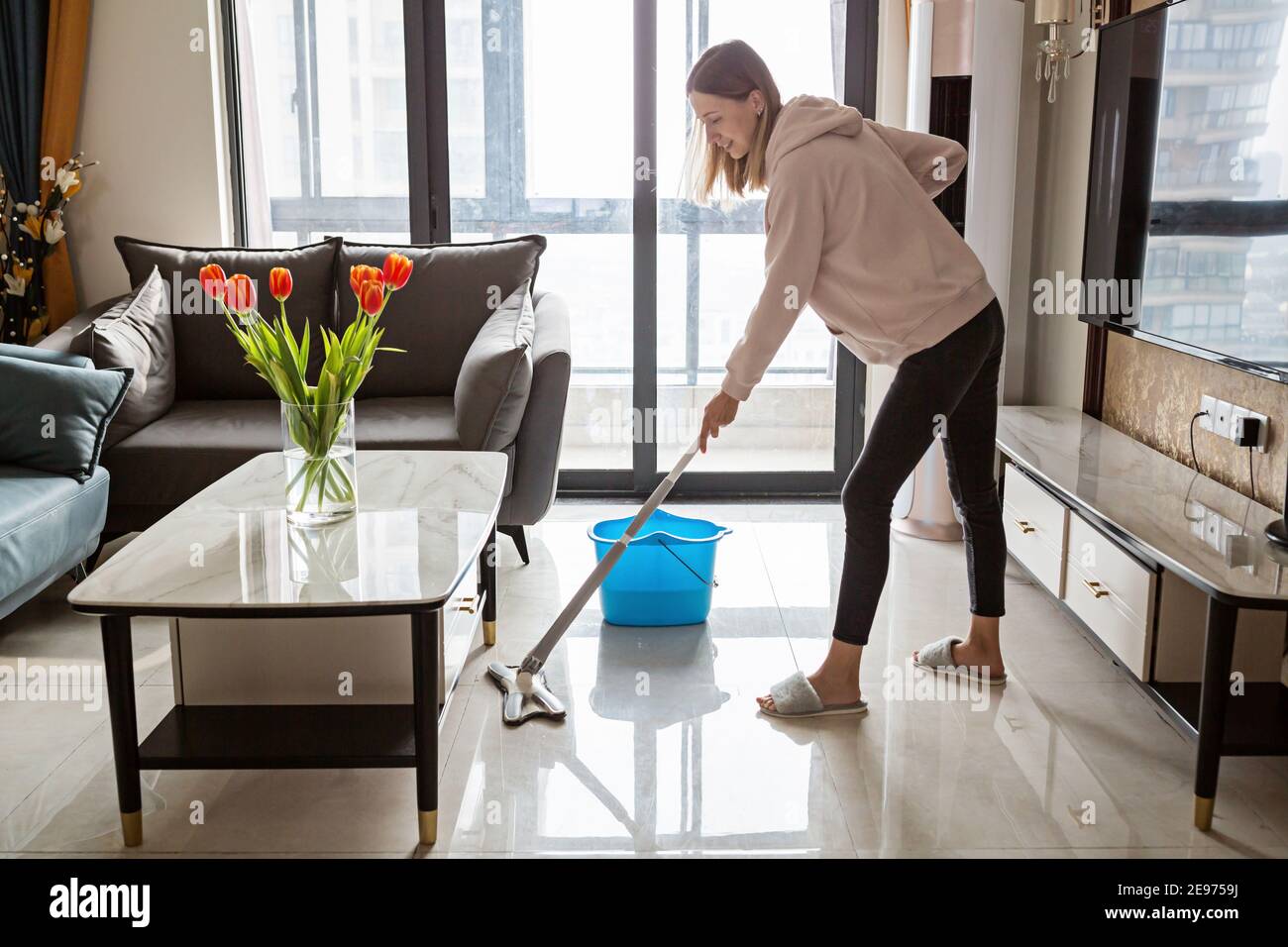 Beautiful young Caucasian blonde housewife cleaning floor in living ...
