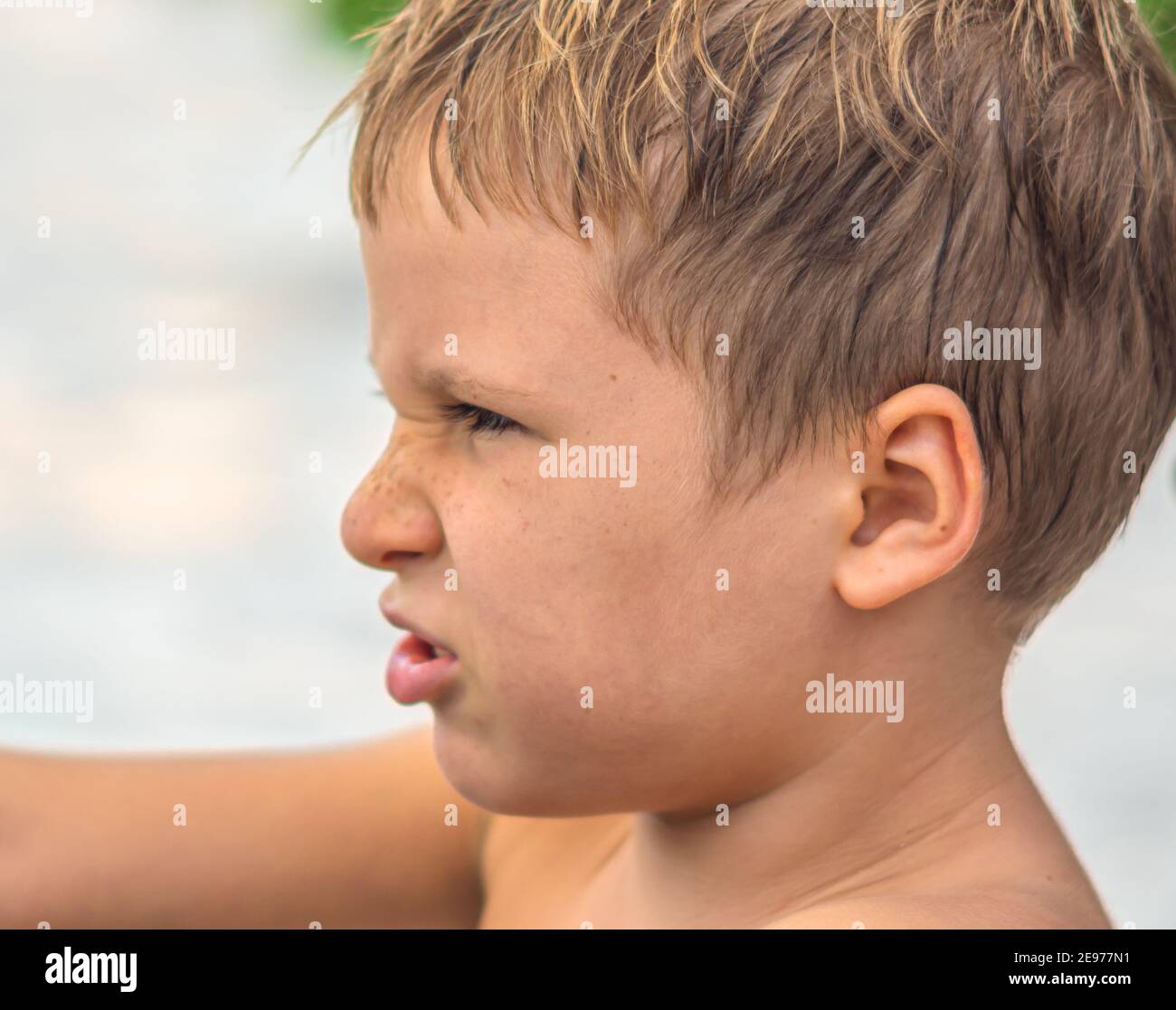 Side portrait mischievous cute blond kid boy, freckled face angry mood ...