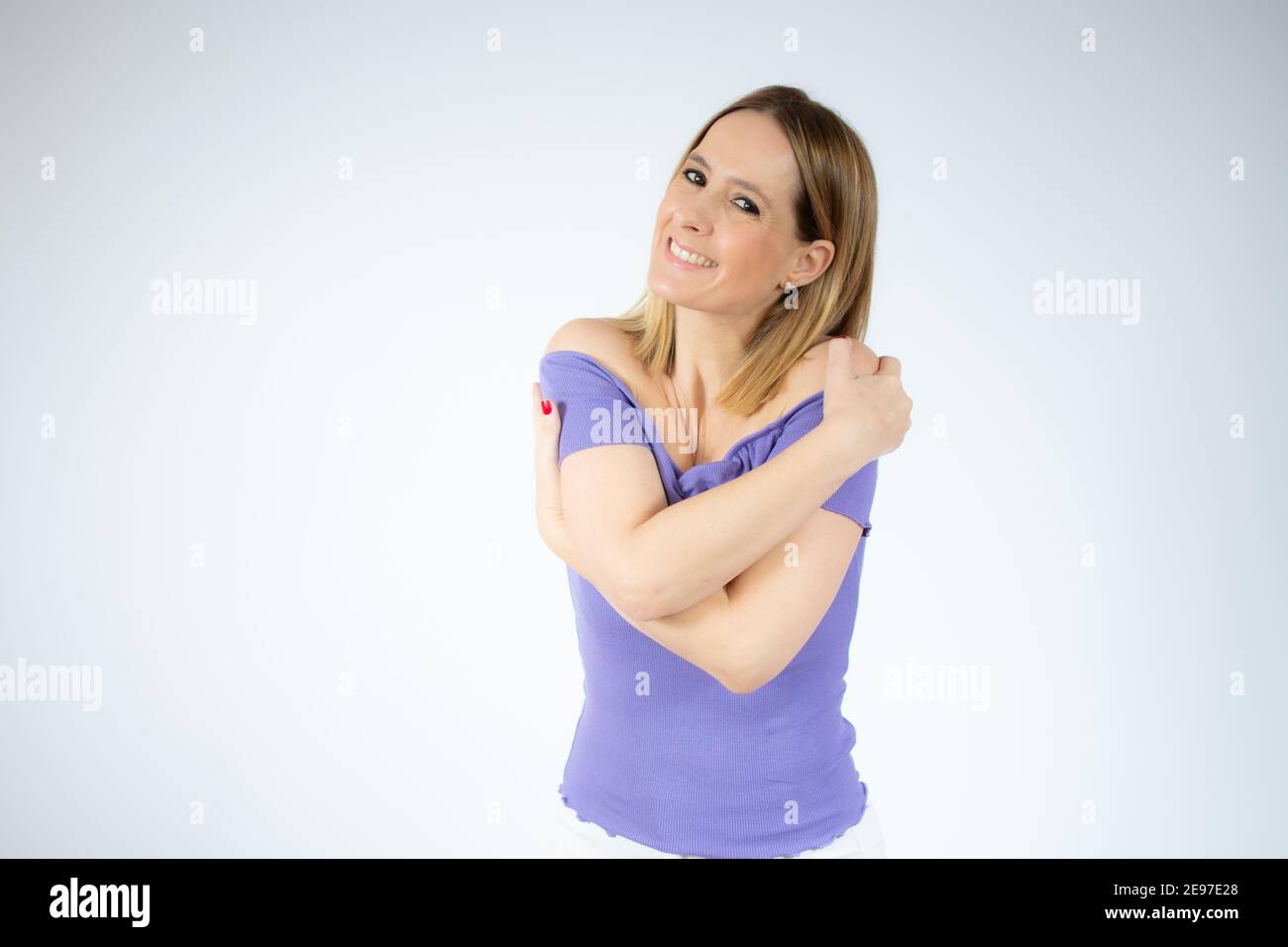 Portrait of a pretty young woman in casual t-shirt hugging herself ...