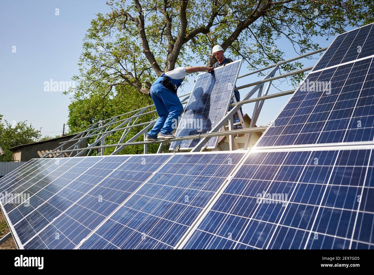 Two workers on tall steel platform mounting heavy solar photo voltaic ...