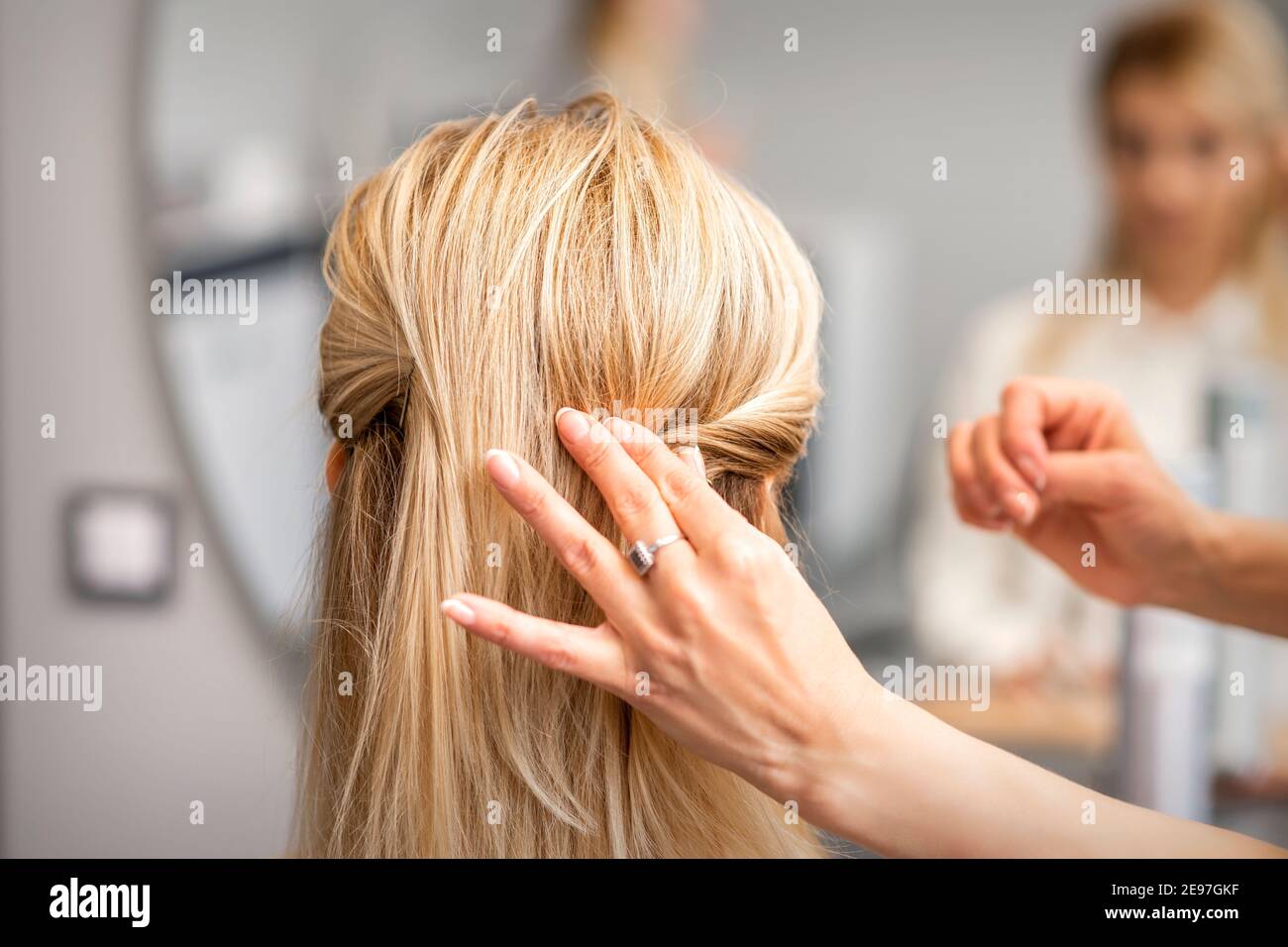 Back view of the female hand of hairdresser models a hairstyle of a ...