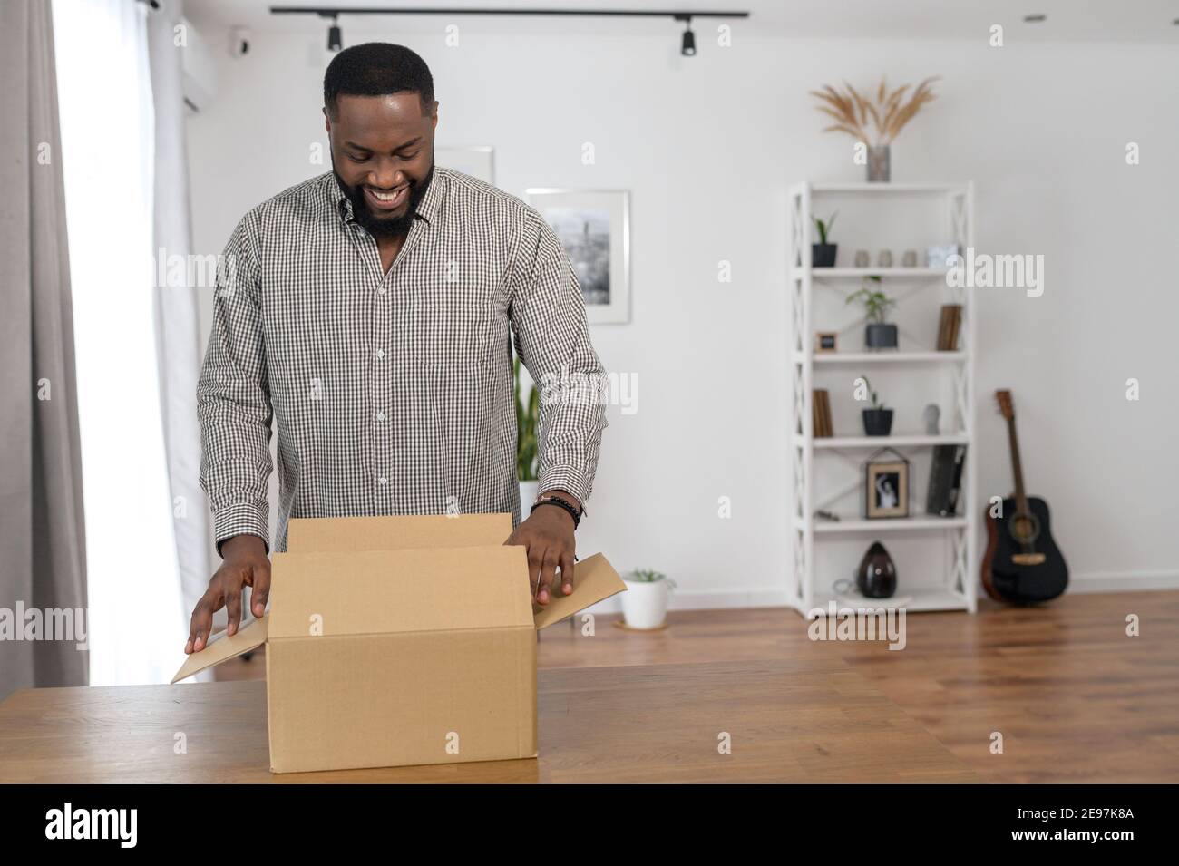 Smiled astonished African millennial looks into parcel box, satisfied ...