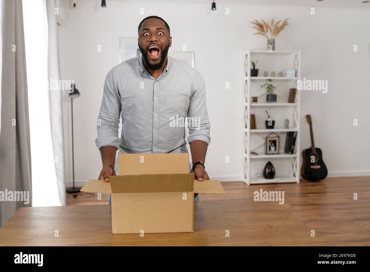 Excited African-American guy screams happily unpacking long awaited ...