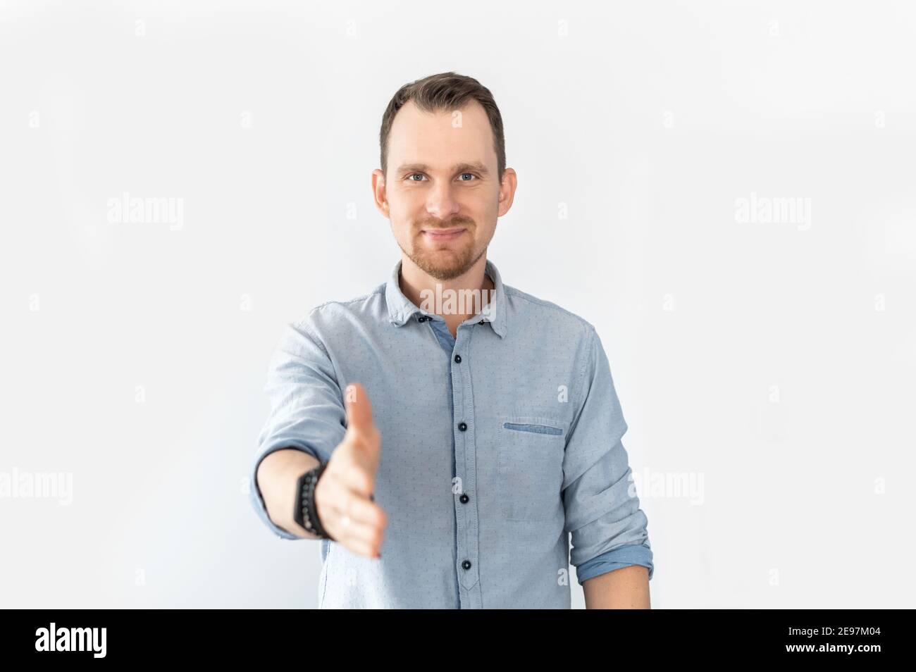 A smiling guy in blue smart casual shirt holds out his hand in ...