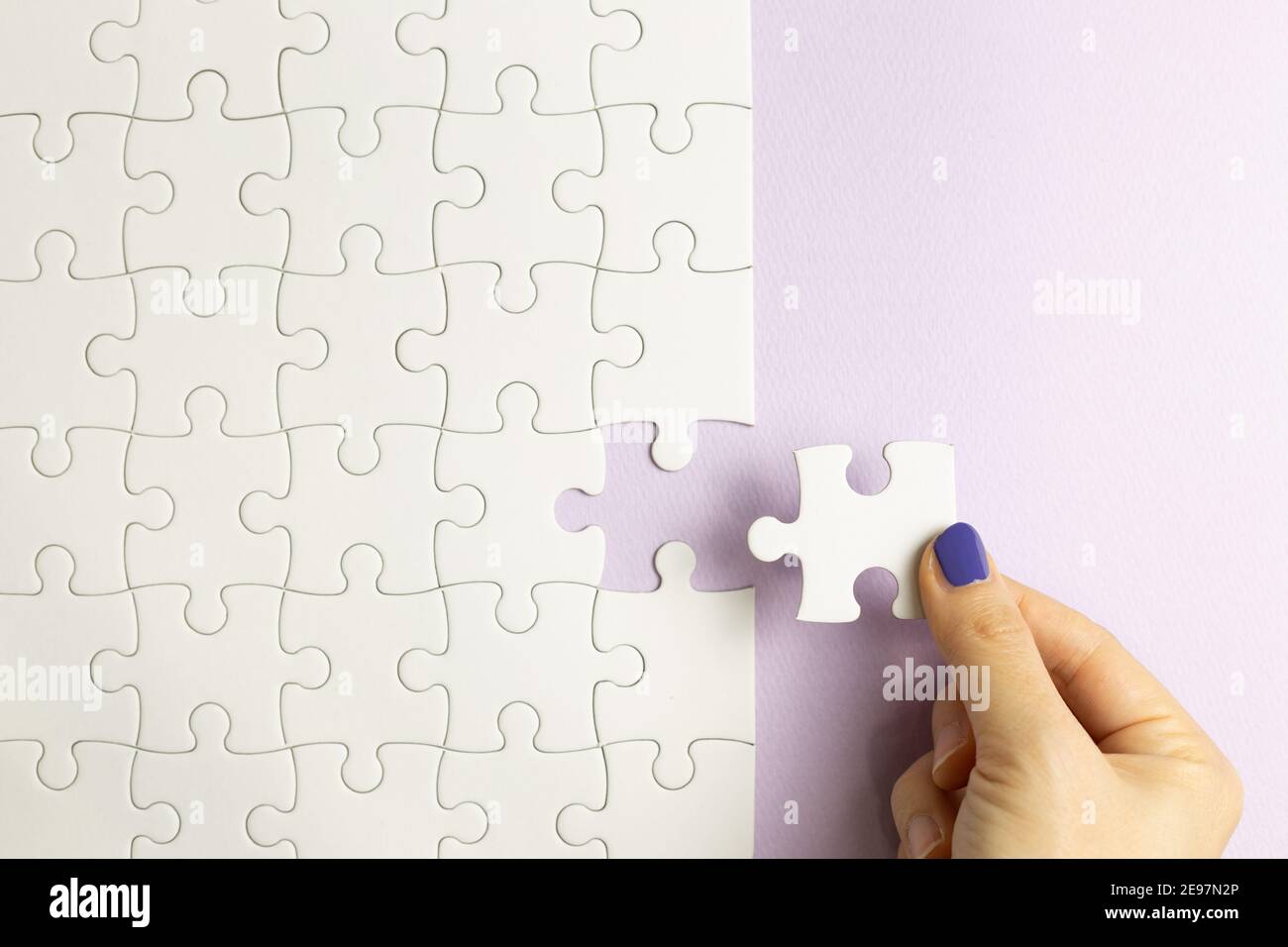 Set of white puzzle pieces and hand holding last one piece on purple ...
