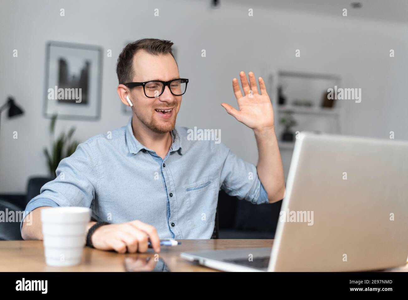 A smiling young man waving hello into webcam, a guy has video call on ...