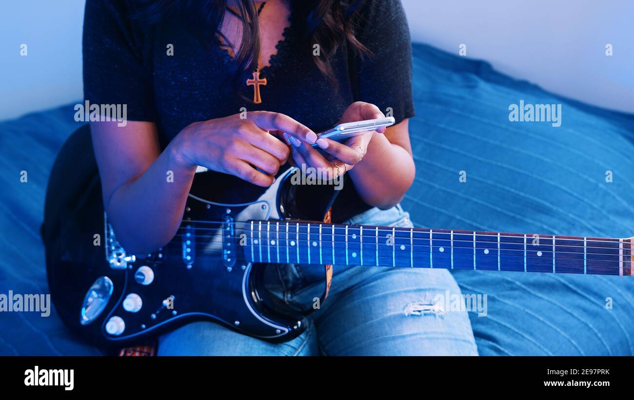 Young woman musician holding acoustic guitar while using smartphone ...