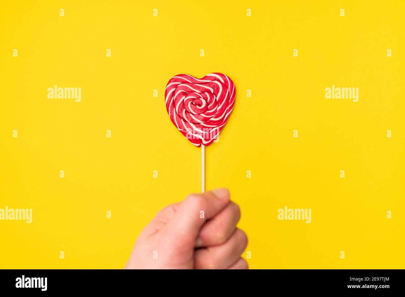 Handholds red heart-shaped lollipop candy isolated on an empty colorful ...
