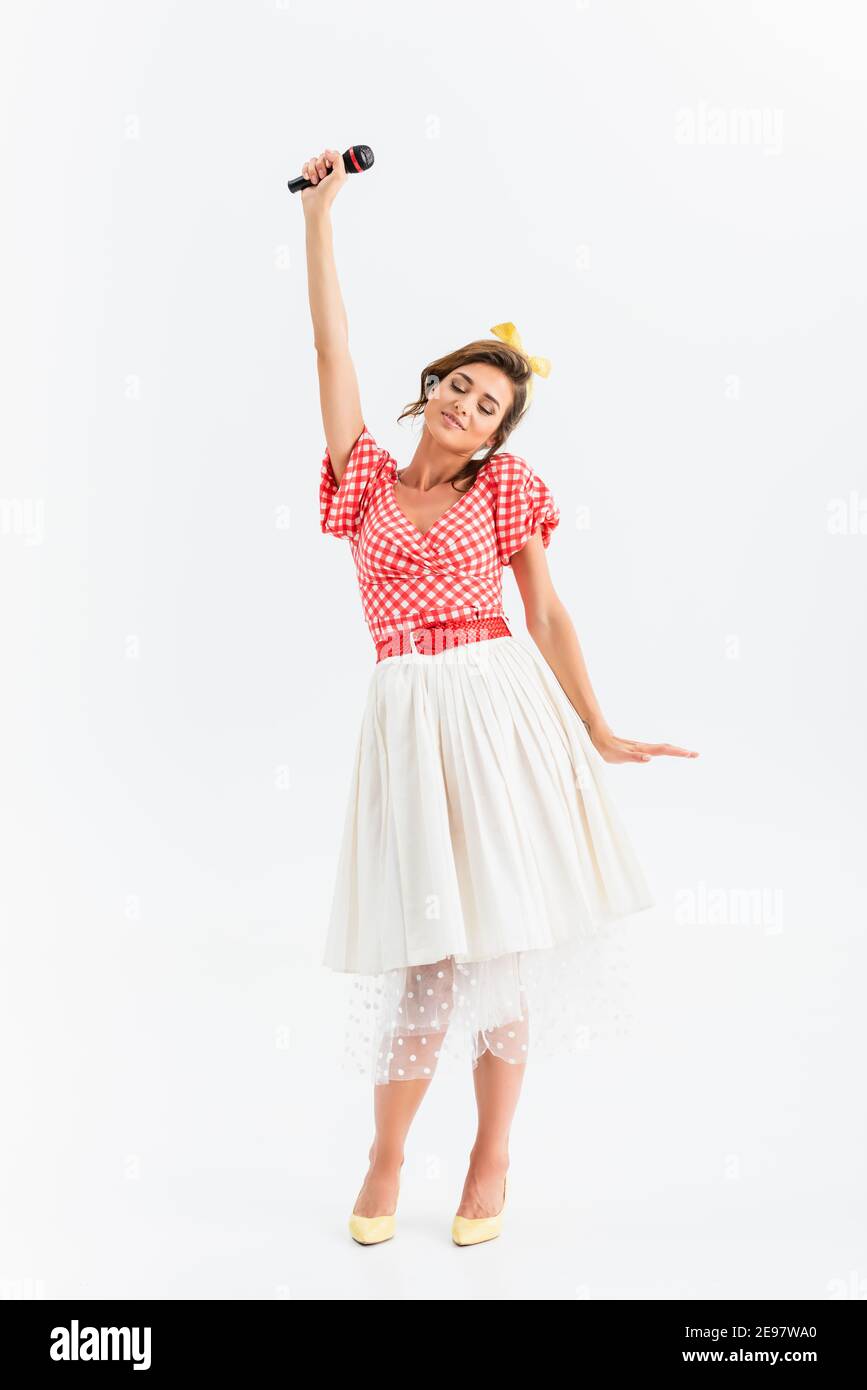full length view of happy pin up woman dancing with microphone on white ...