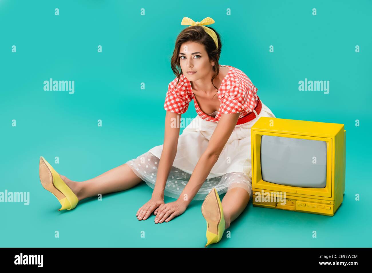 pretty pin up woman sitting on floor near bright yellow vintage tv and ...