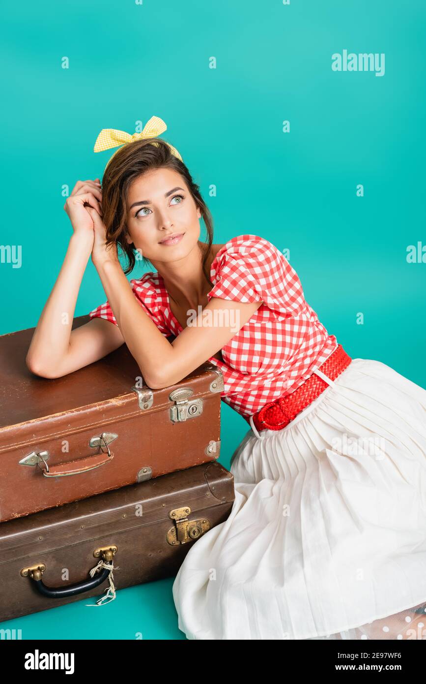 smiling, dreamy pin up woman leaning on vintage suitcases on turquoise ...