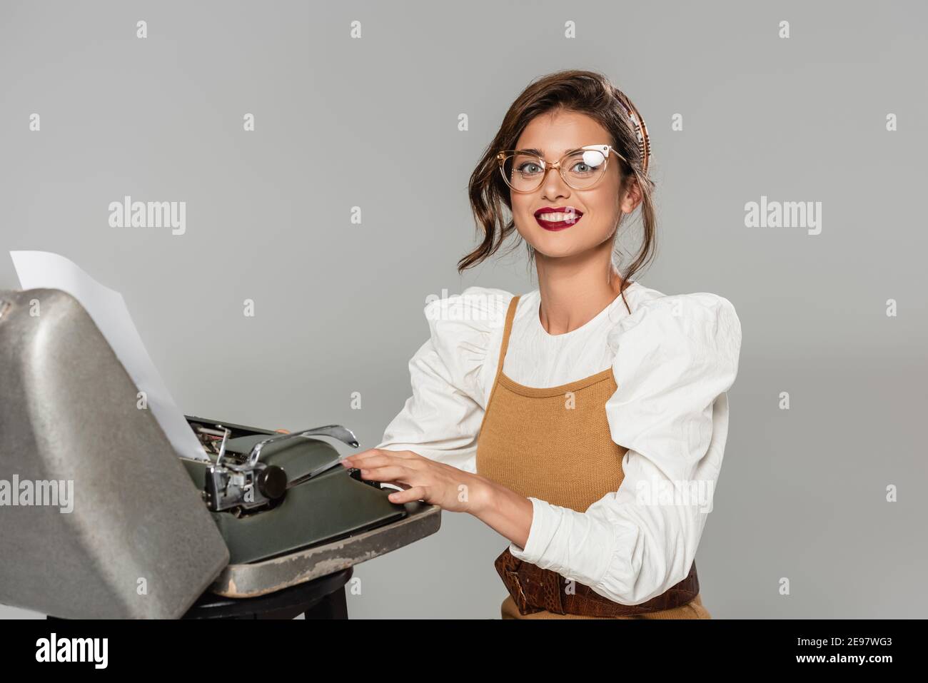 cheerful secretary typing on retro typewriter and smiling at camera ...