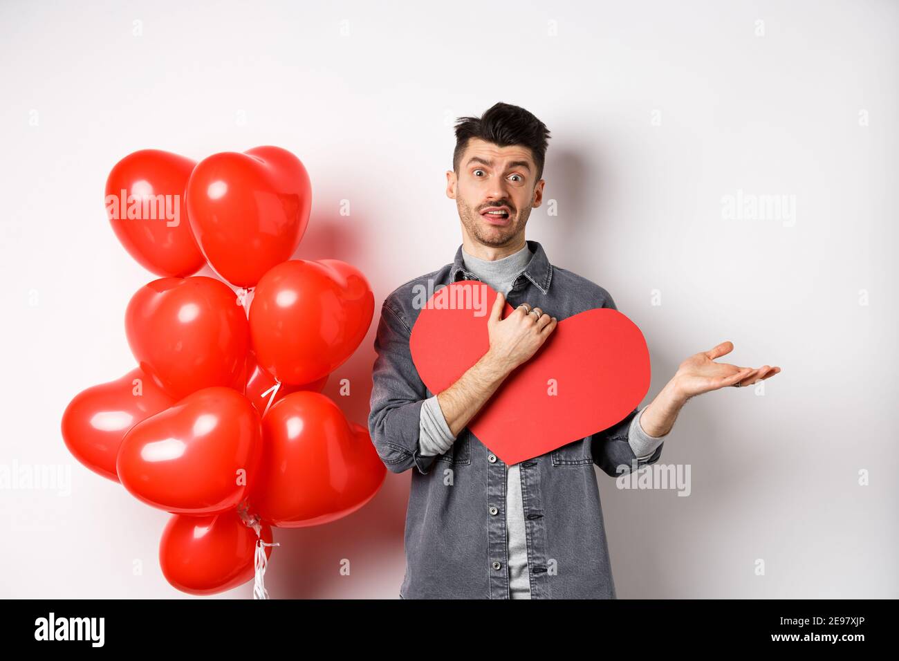 Confused man hugging big Valentine card and shrugging, feeling careless ...