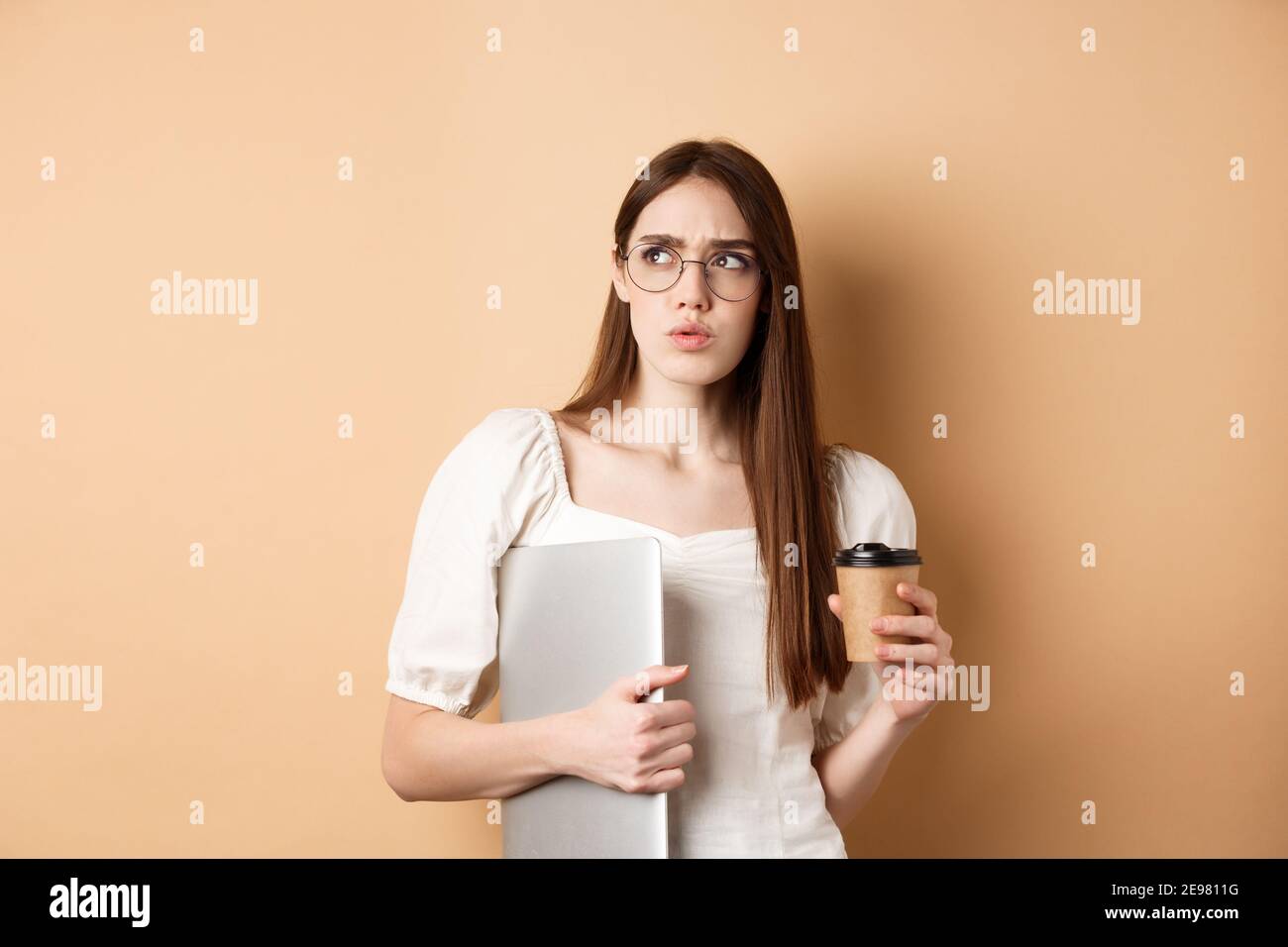 Confused and pensive girl with laptop looking aside suspicious ...