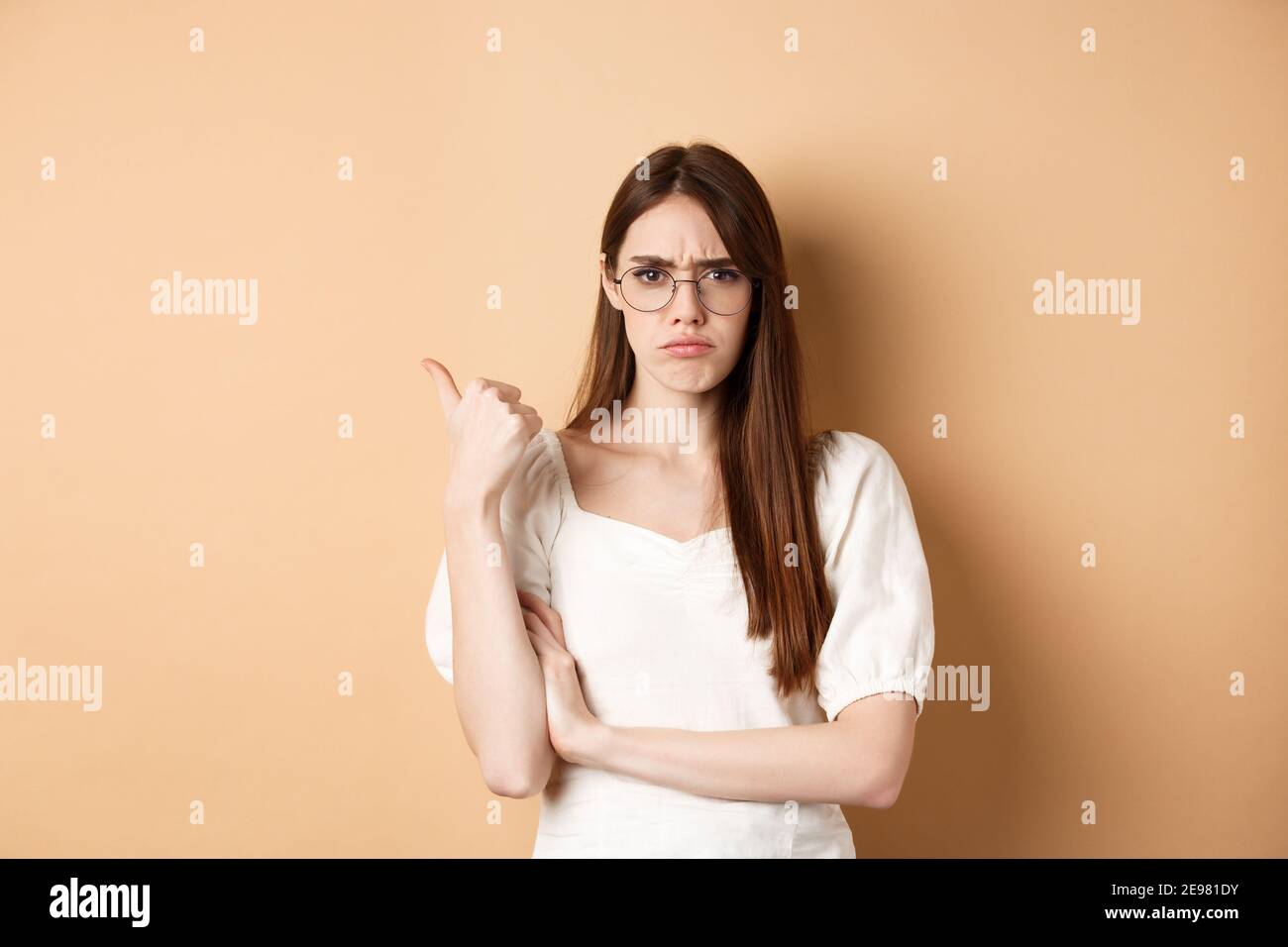 Disappointed girl in glasses frowning, pointing aside at bad product ...