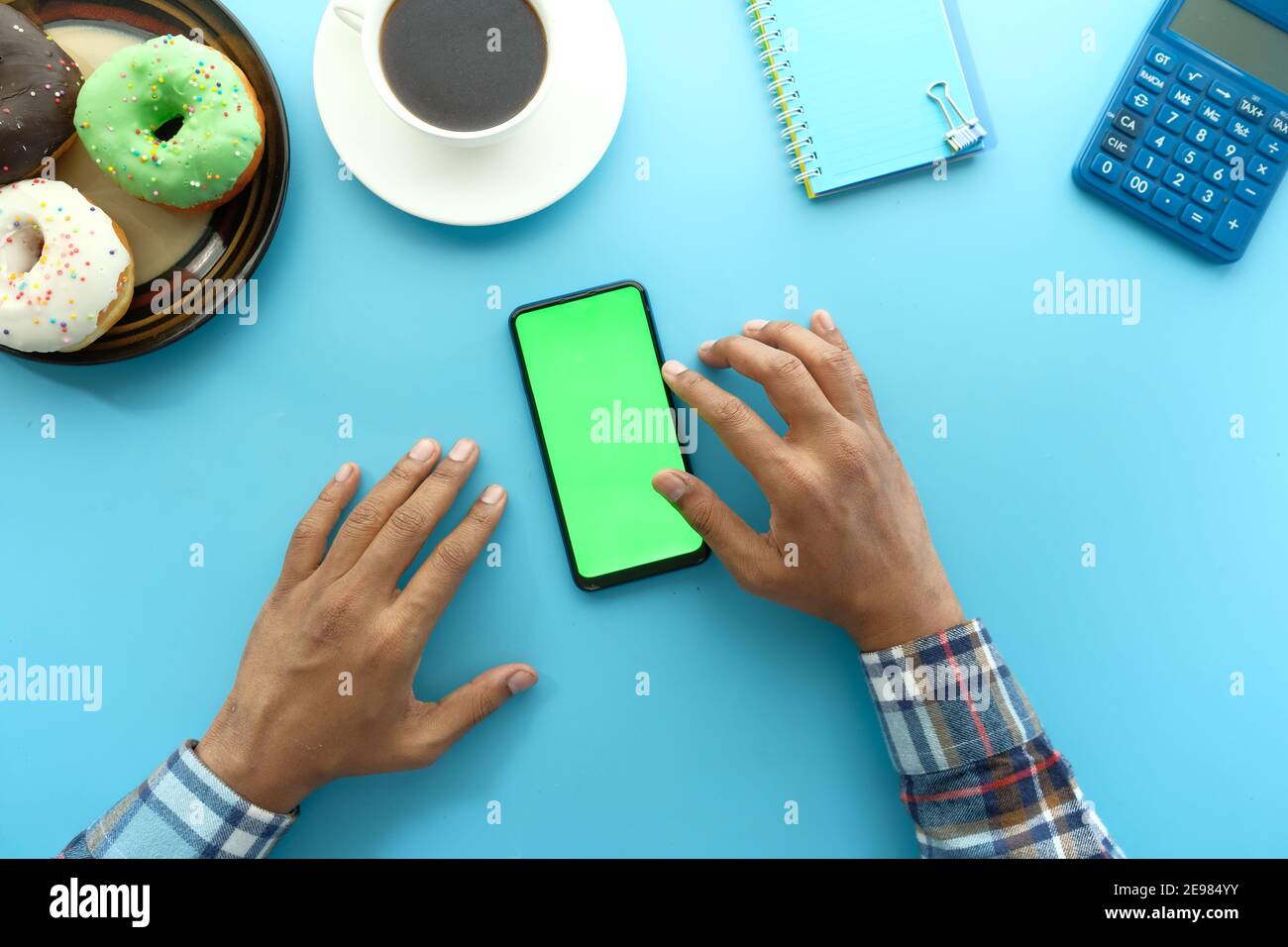 top view of man hand using smart phone with donuts, tea blue background ...
