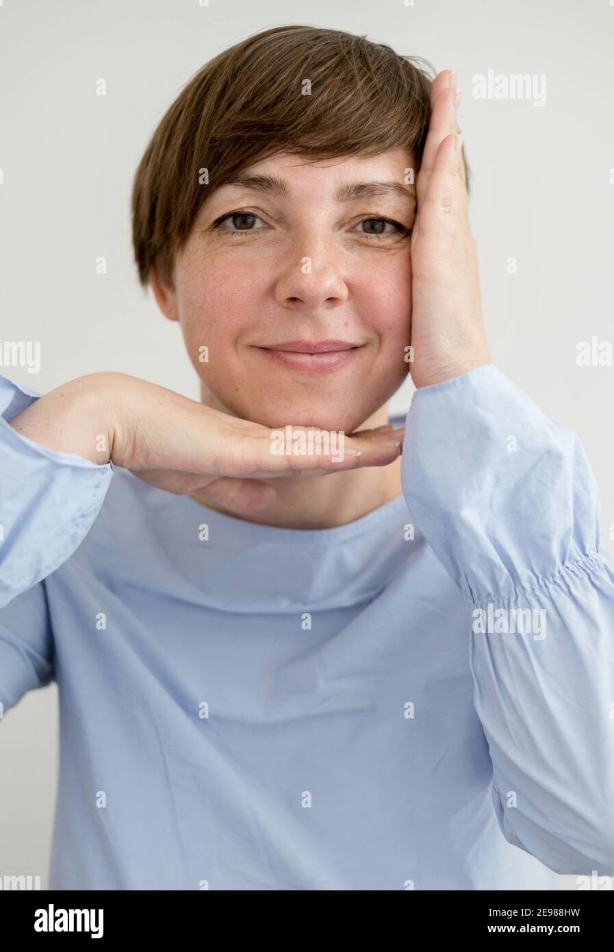 Close-up portrait of a short-haired woman, holding hands by the face ...