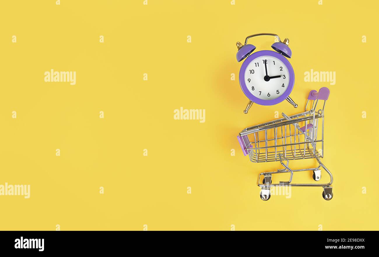 Supermarket trolley and violet alarm clock on yellow background with ...